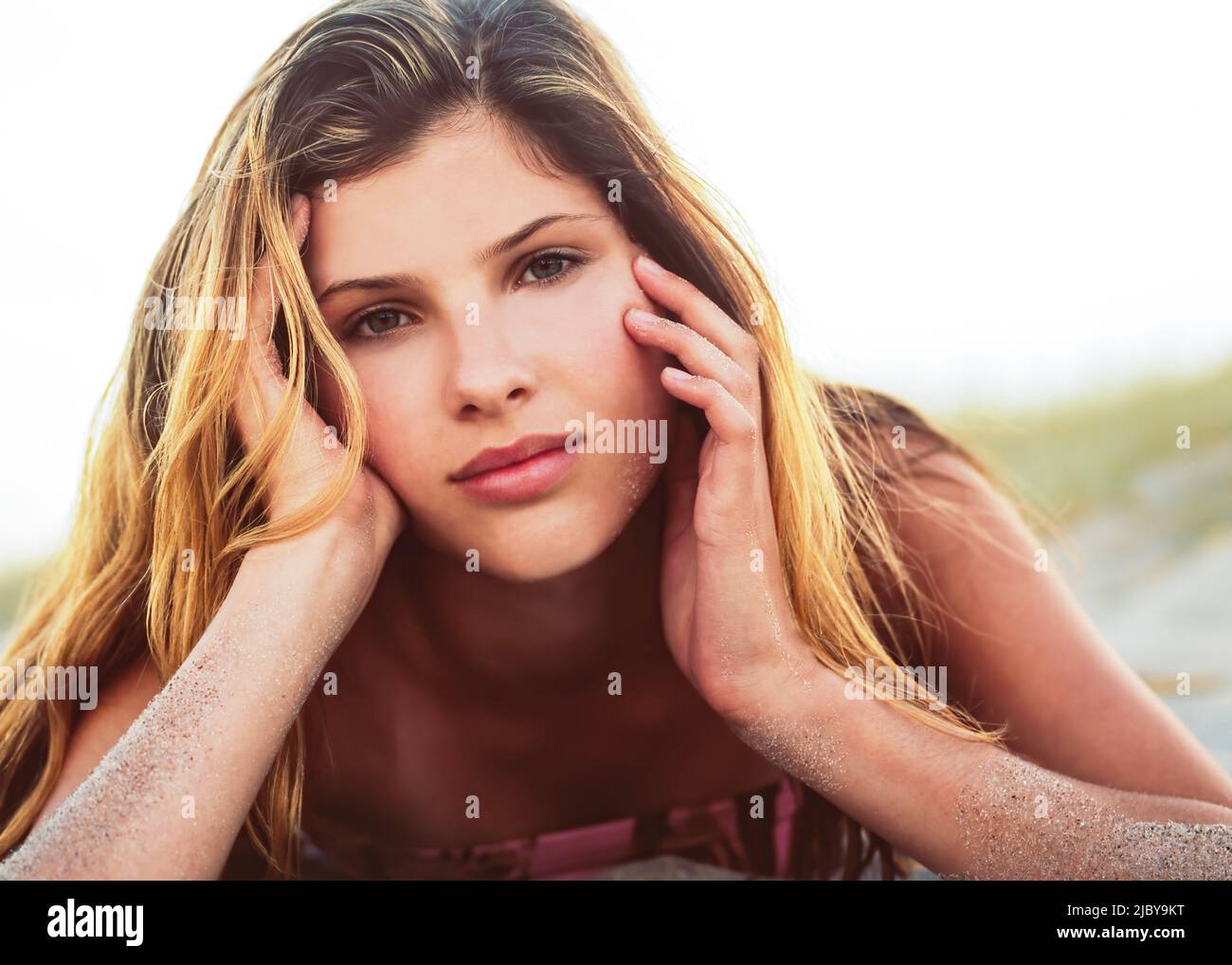 Portrait of young woman resting head on hands laying down in the sand ...