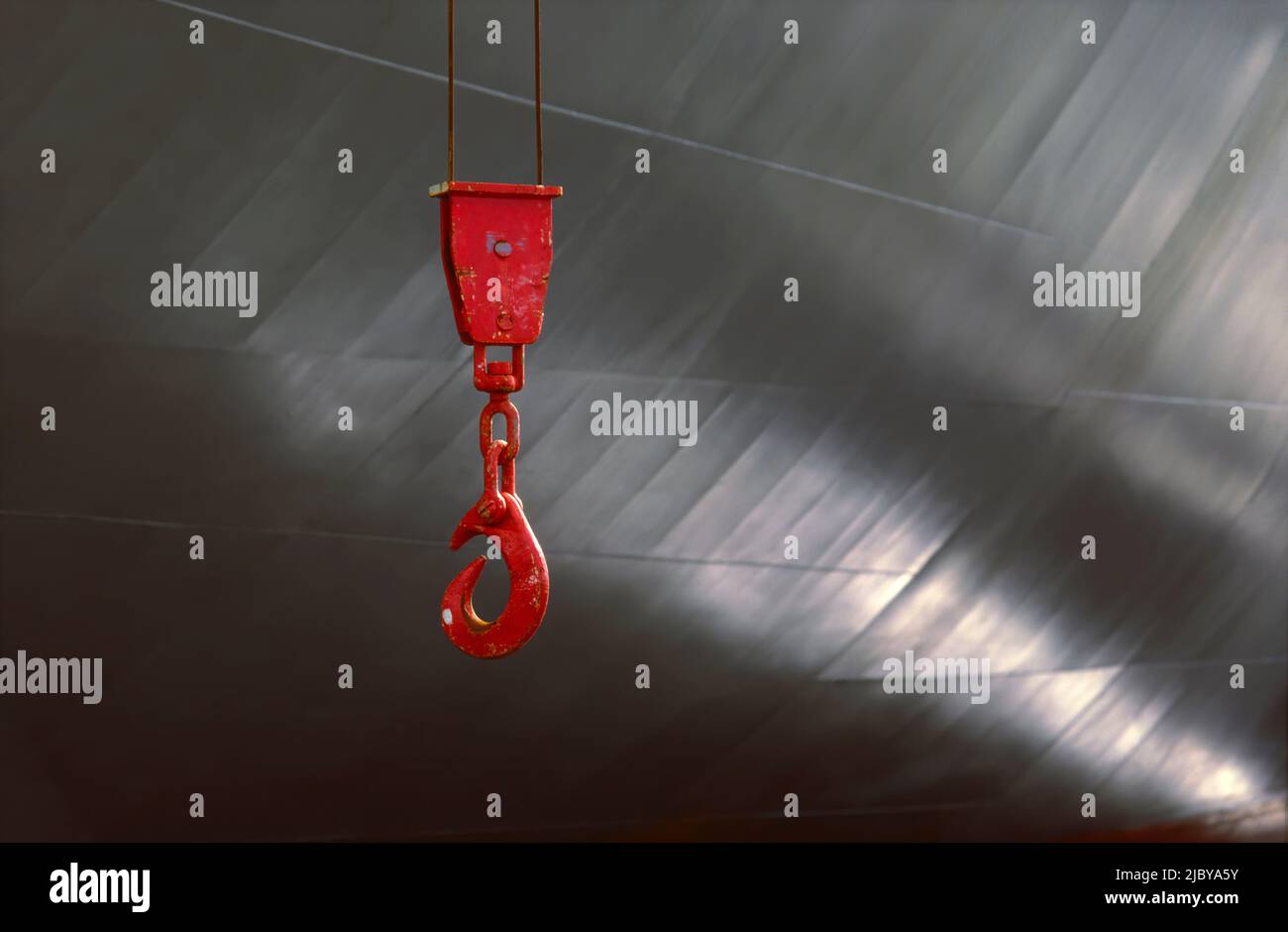 Large red winch hook against side of ship and reflections from water ...
