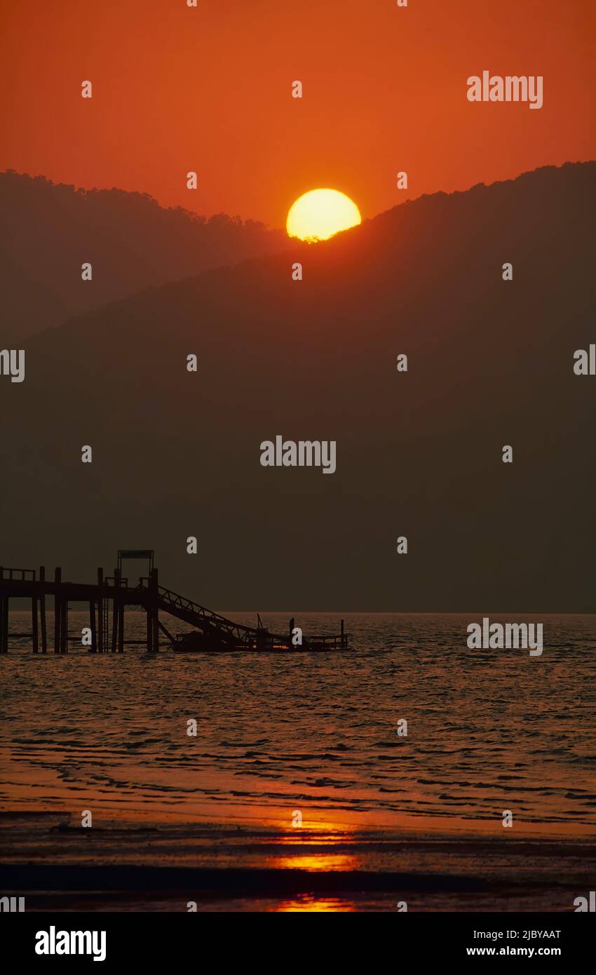 Sun setting behind the hills and Jetty on water Stock Photo - Alamy