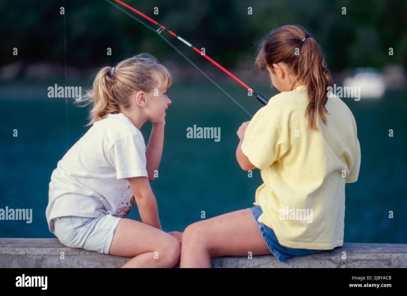 Two young girls fishing off jetty Stock Photo - Alamy