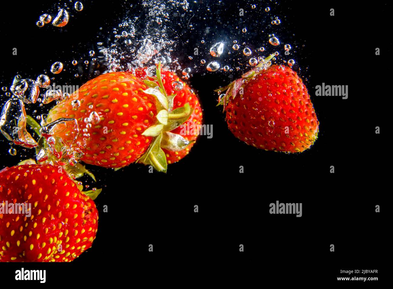 ripe strawberries fall into the water, raising splashes and air bubbles ...