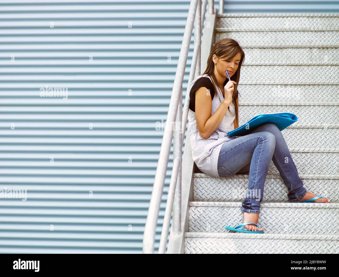 Female student sitting on metal staircase writing in folder Stock Photo ...