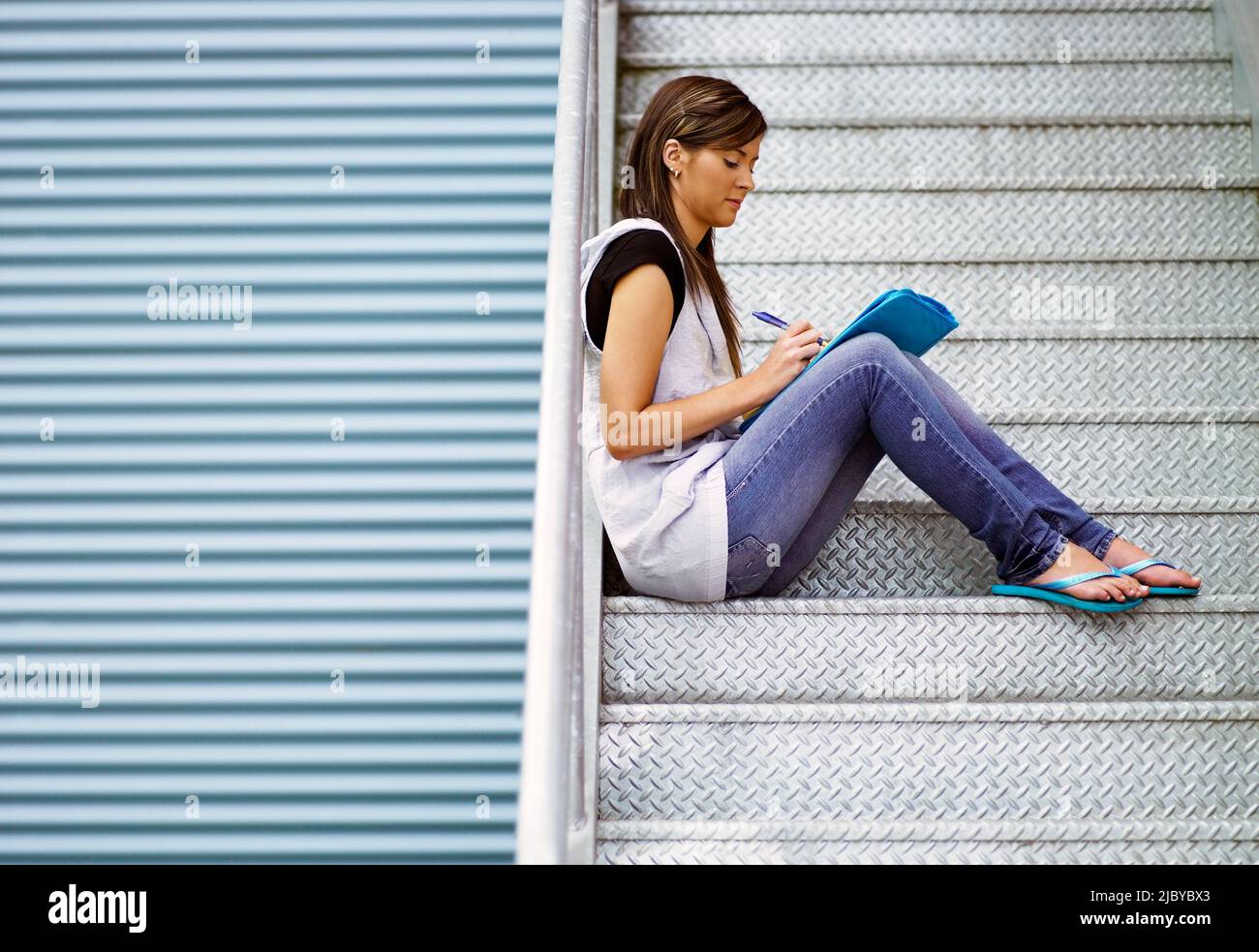 Female student sitting on metal staircase writing in folder Stock Photo ...