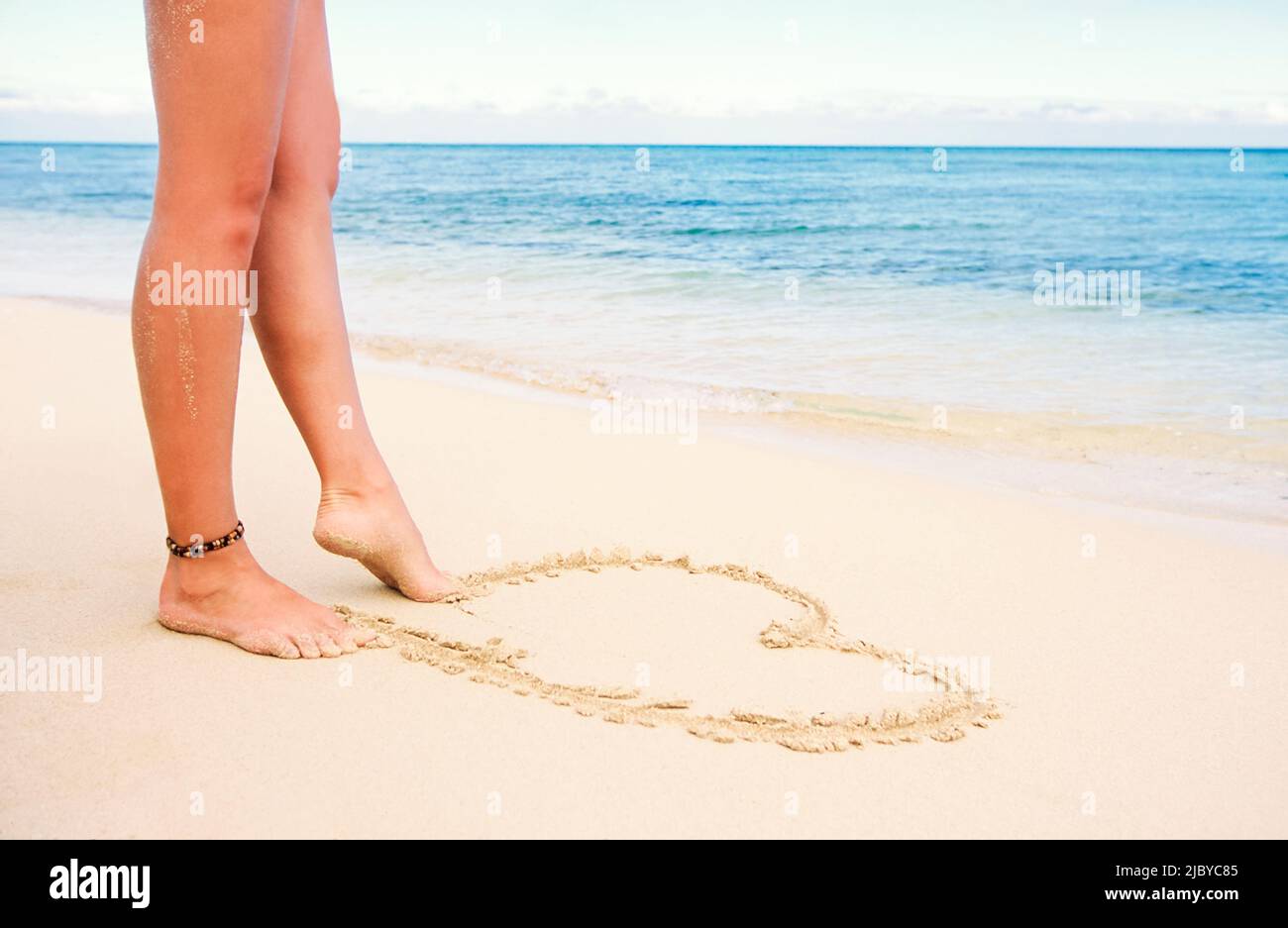 Close up of woman's sandy feet drawing a heart in the sand on tropical ...