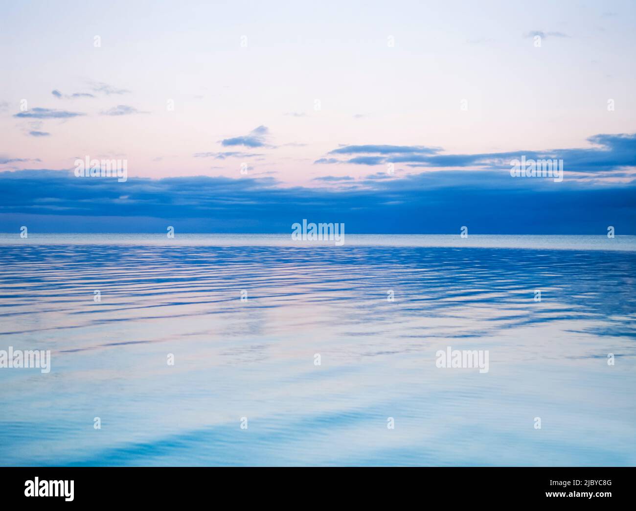 Sky meets sea on horizon line and clouds reflected in the calm rippling ...