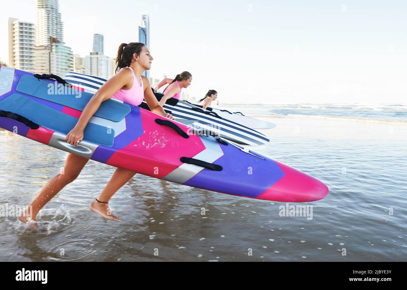 Team of female surf lifeguards training and running into sea holding ...