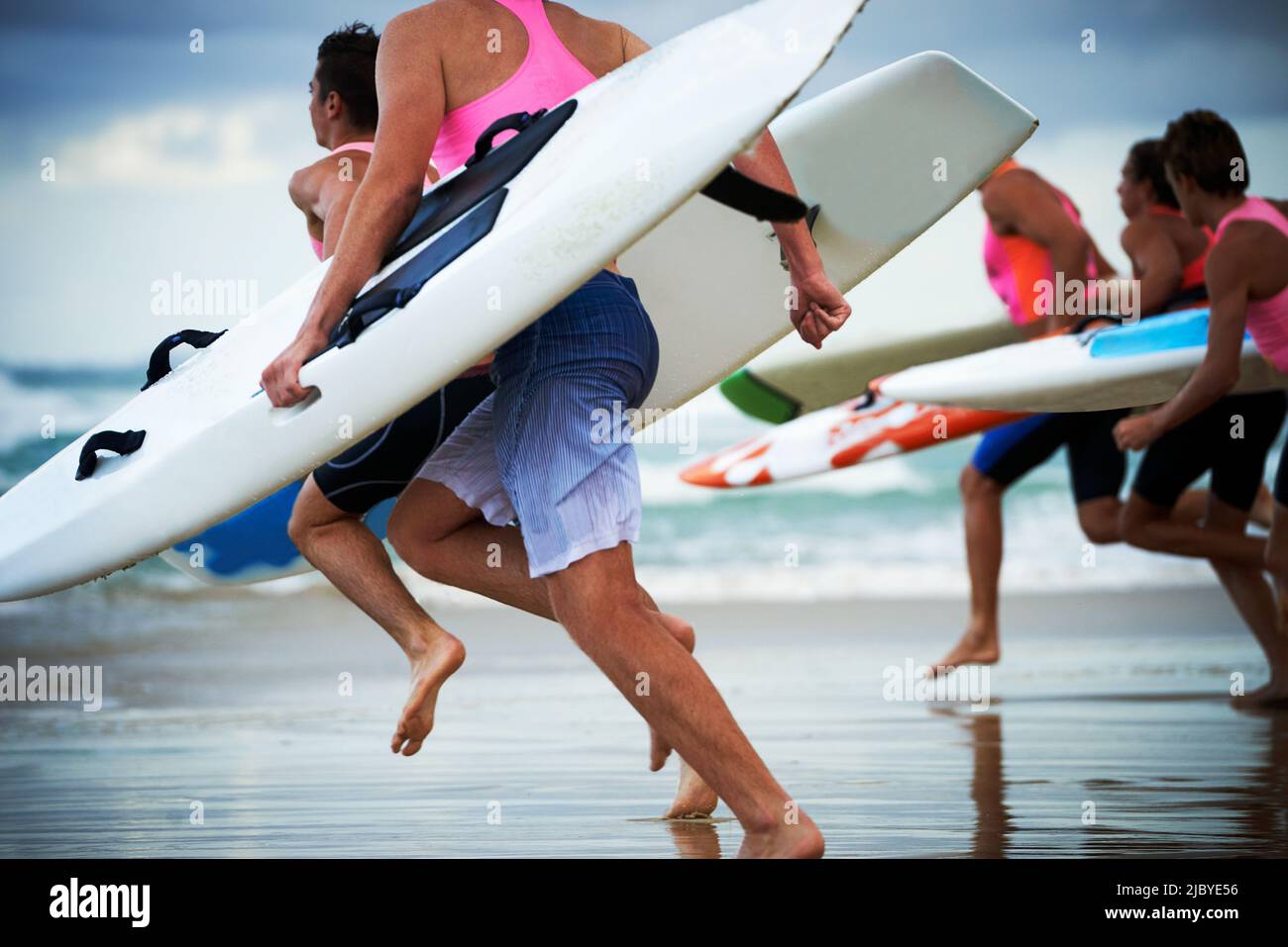 Close up of team of male surf lifeguards training and running into sea ...
