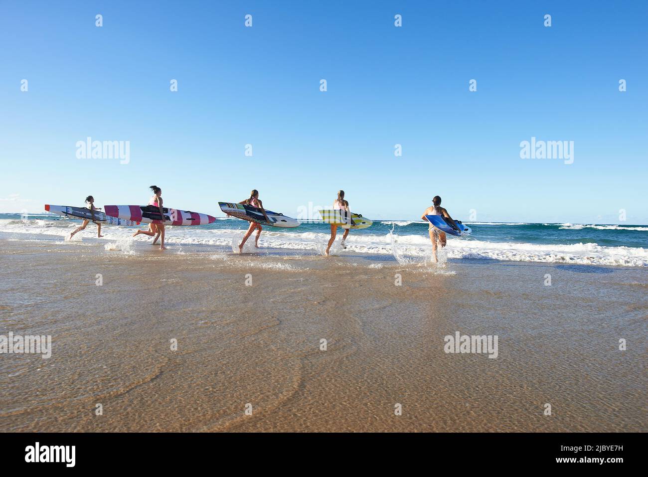 Back view of team of female surf lifeguards training and running into ...