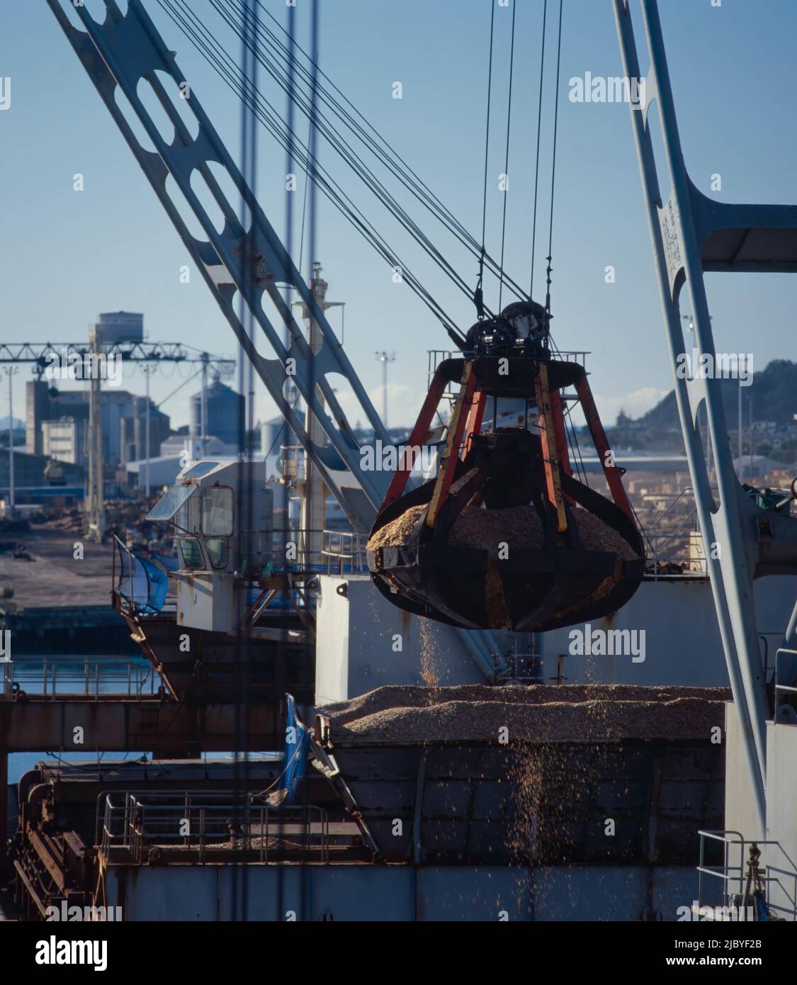 Close up of large claw bucket loading wood chips onto ship at port ...