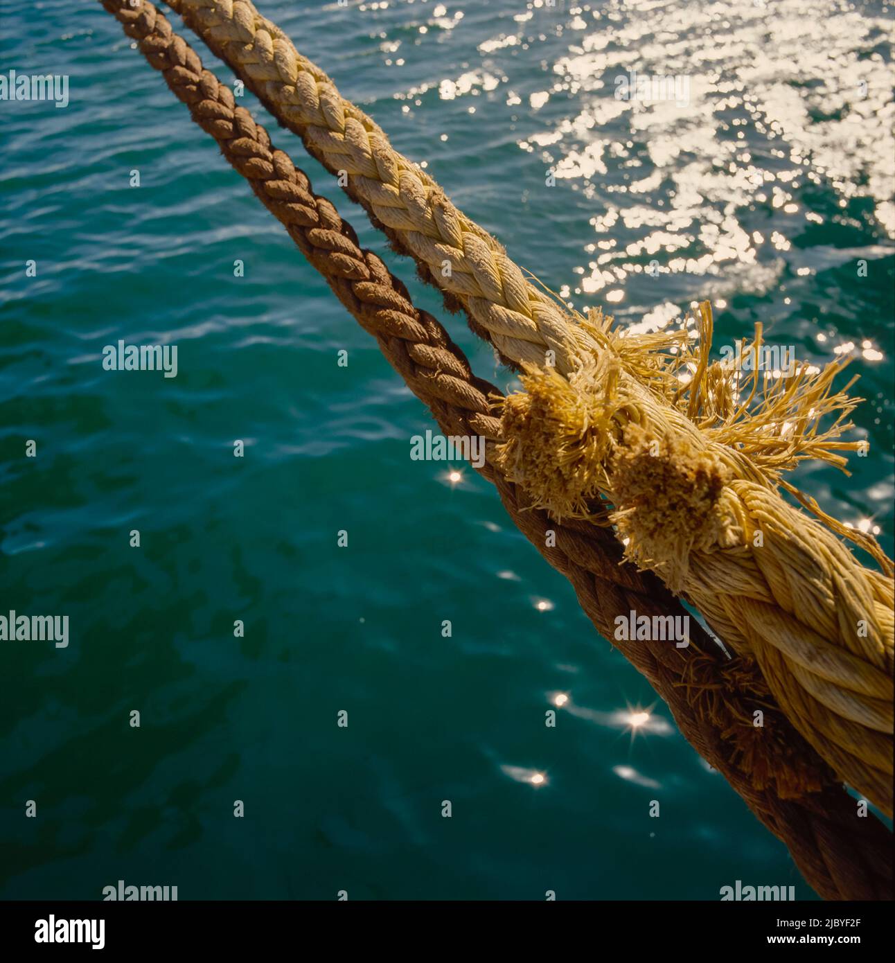 Thick ship's ropes securing ship to wharf against sparkling water Stock ...