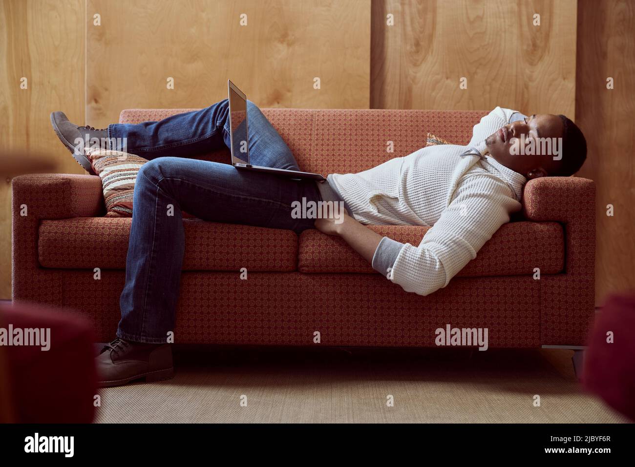 Young man taking a nap on loveseat with his computer on his lap Stock ...