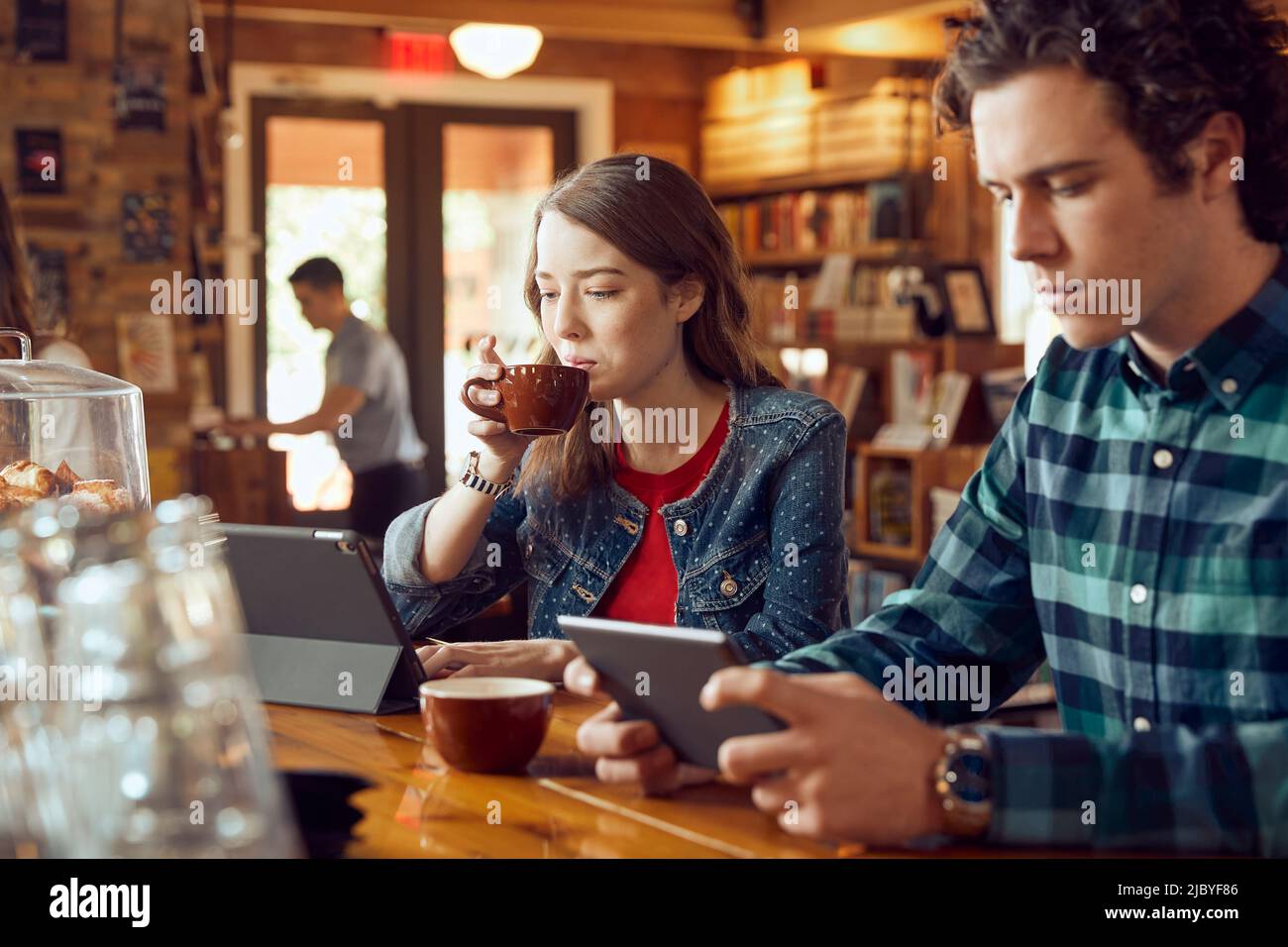 Young man and woman sitting at counter in cafe bookstore using digital ...