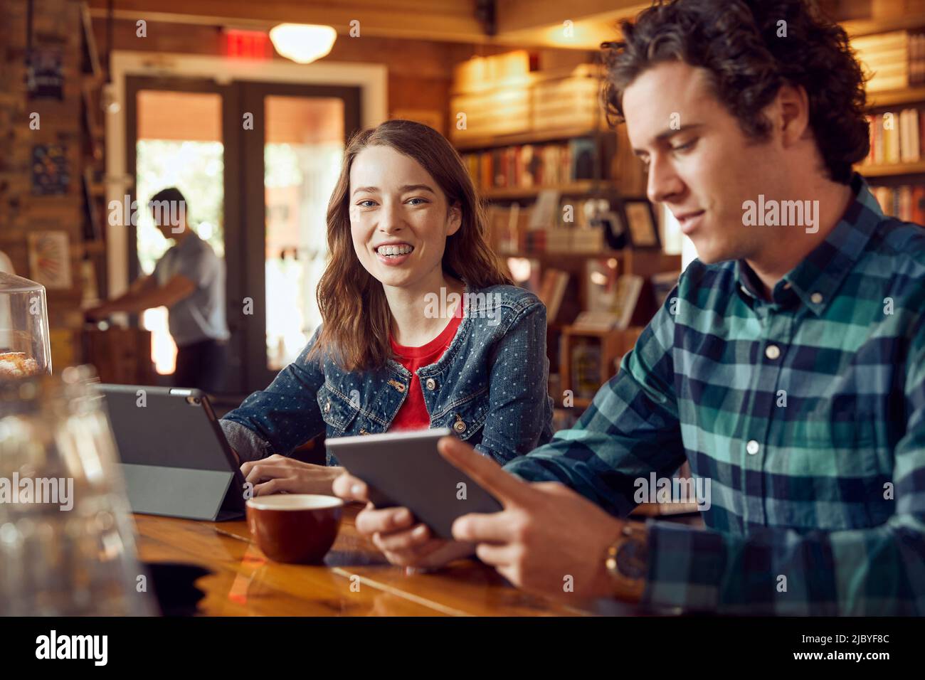 Young man and woman sitting at counter in cafe bookstore using digital ...