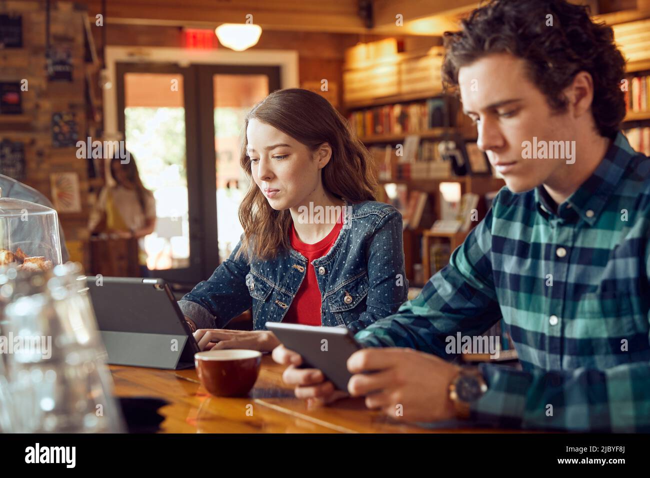 Young man and woman sitting at counter in cafe bookstore using digital ...
