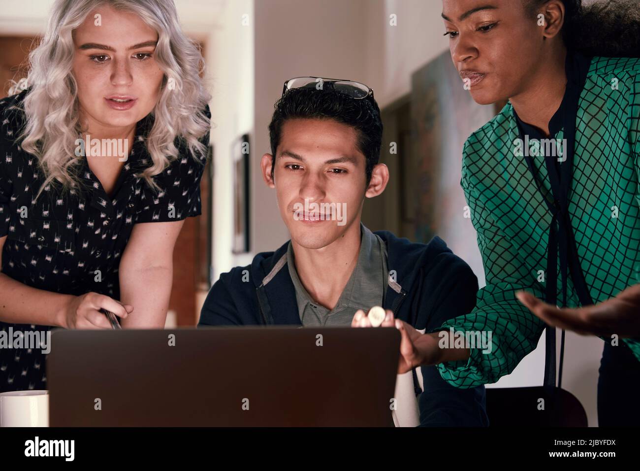 Group of young co-workers gathered around laptop computer looking at ...