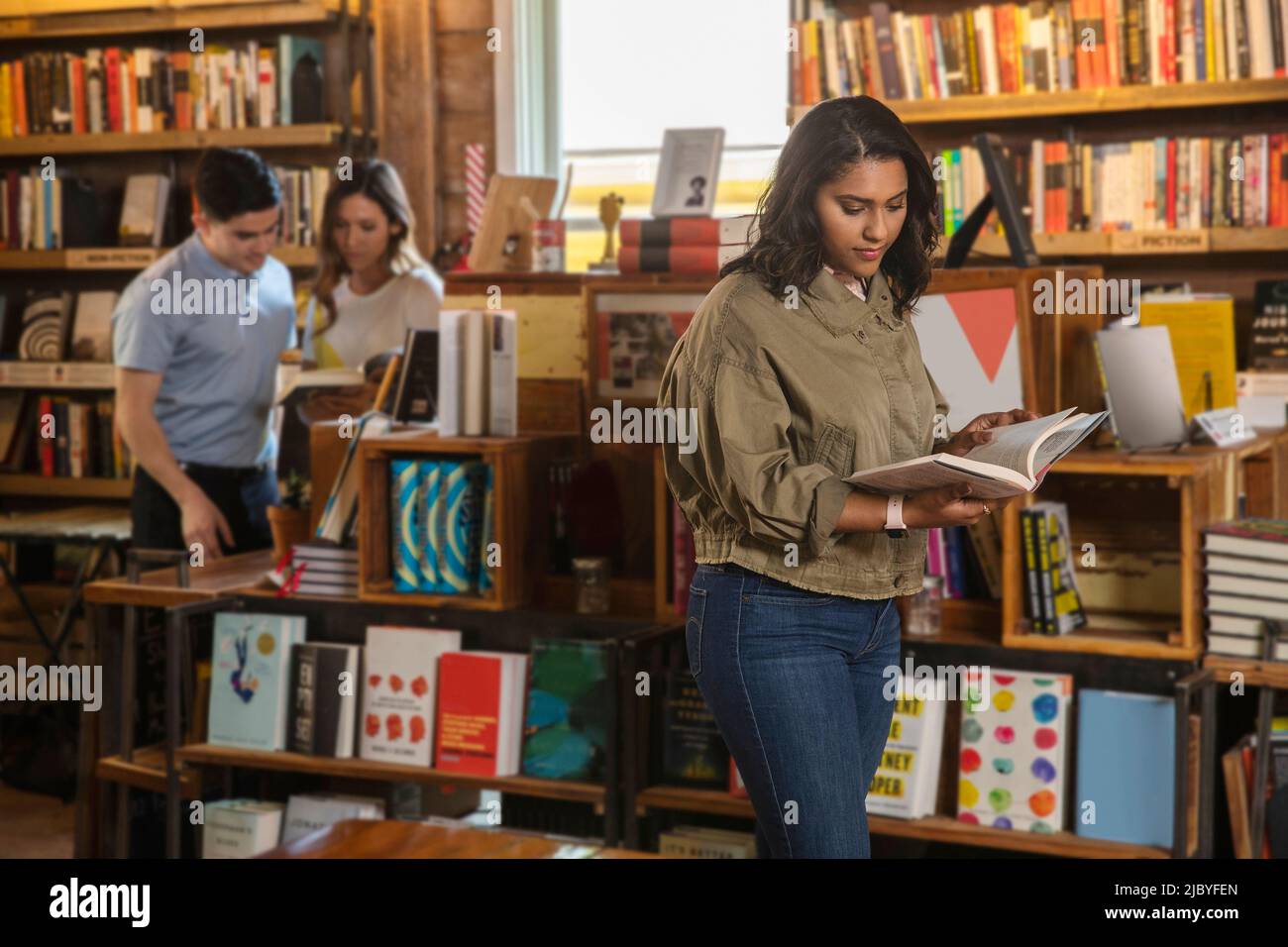 Portrait of young woman looking through book in boutique book store ...