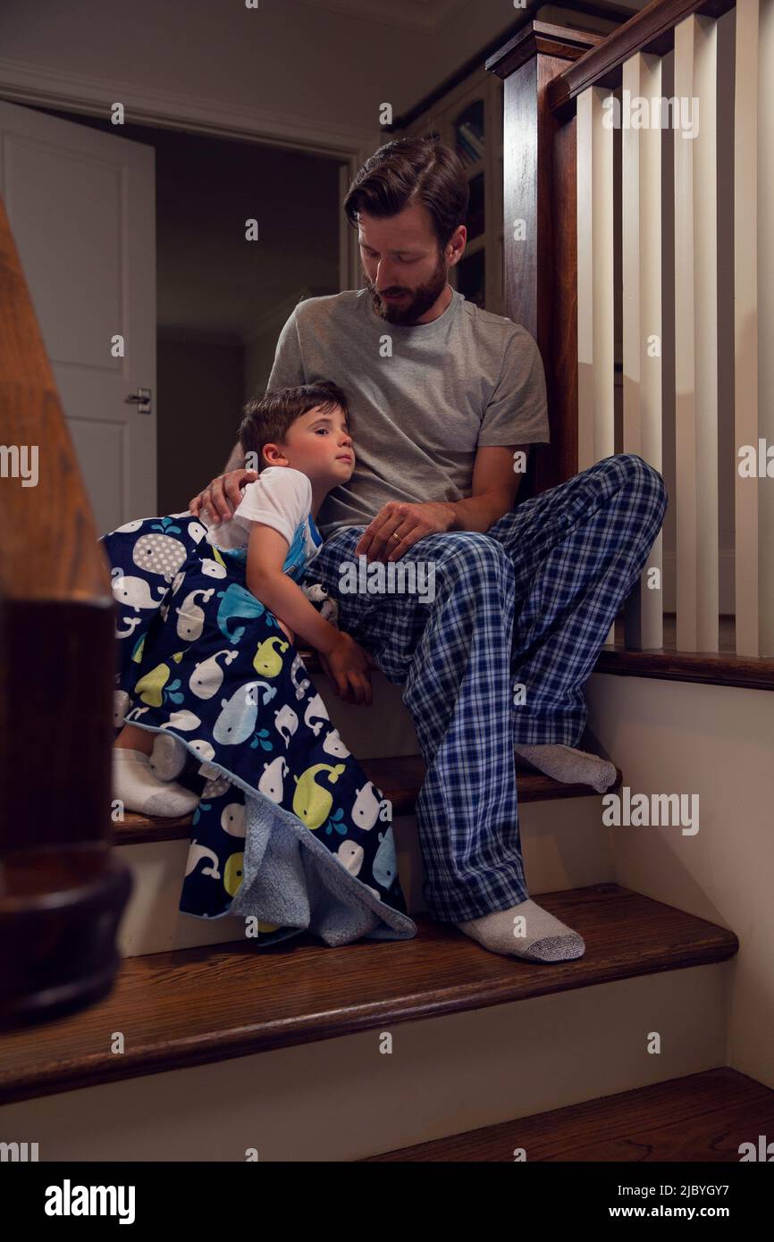 Father and son sitting at top of stairs in home getting ready for ...