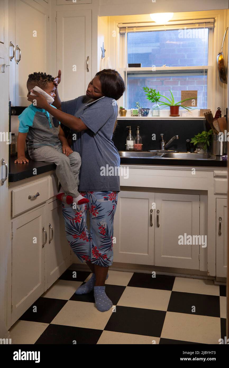 Mom at home in kitchen with son sitting on counter checking his ...