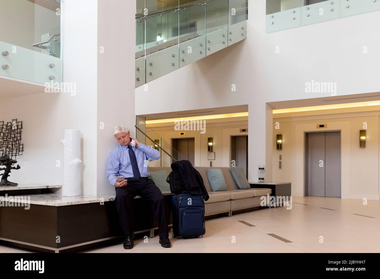Mature Caucasian man sitting in hotel lobby with luggage, looking at ...
