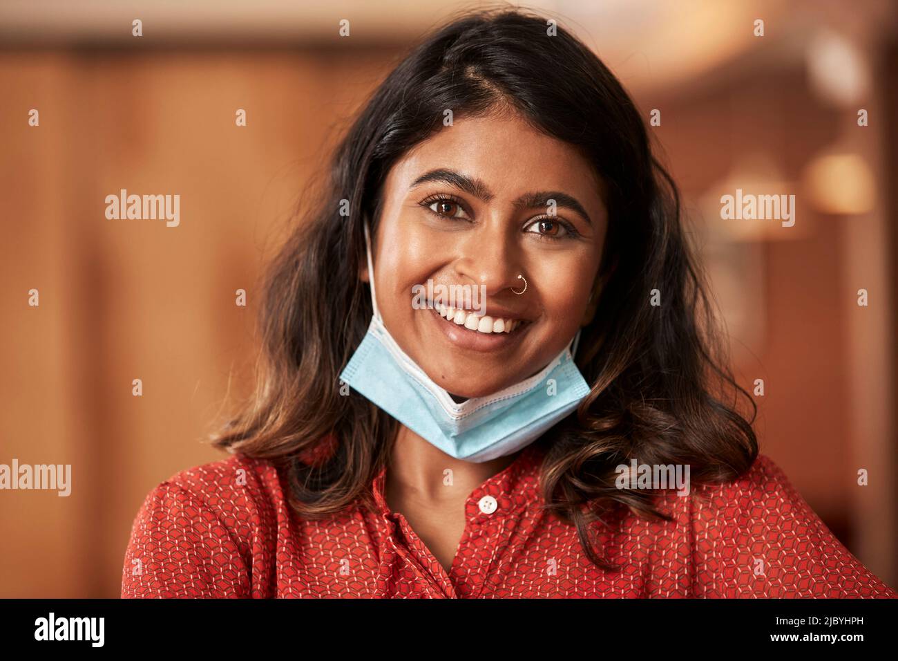 Portrait of young ethnic woman wearing face mask pulled down to reveal ...