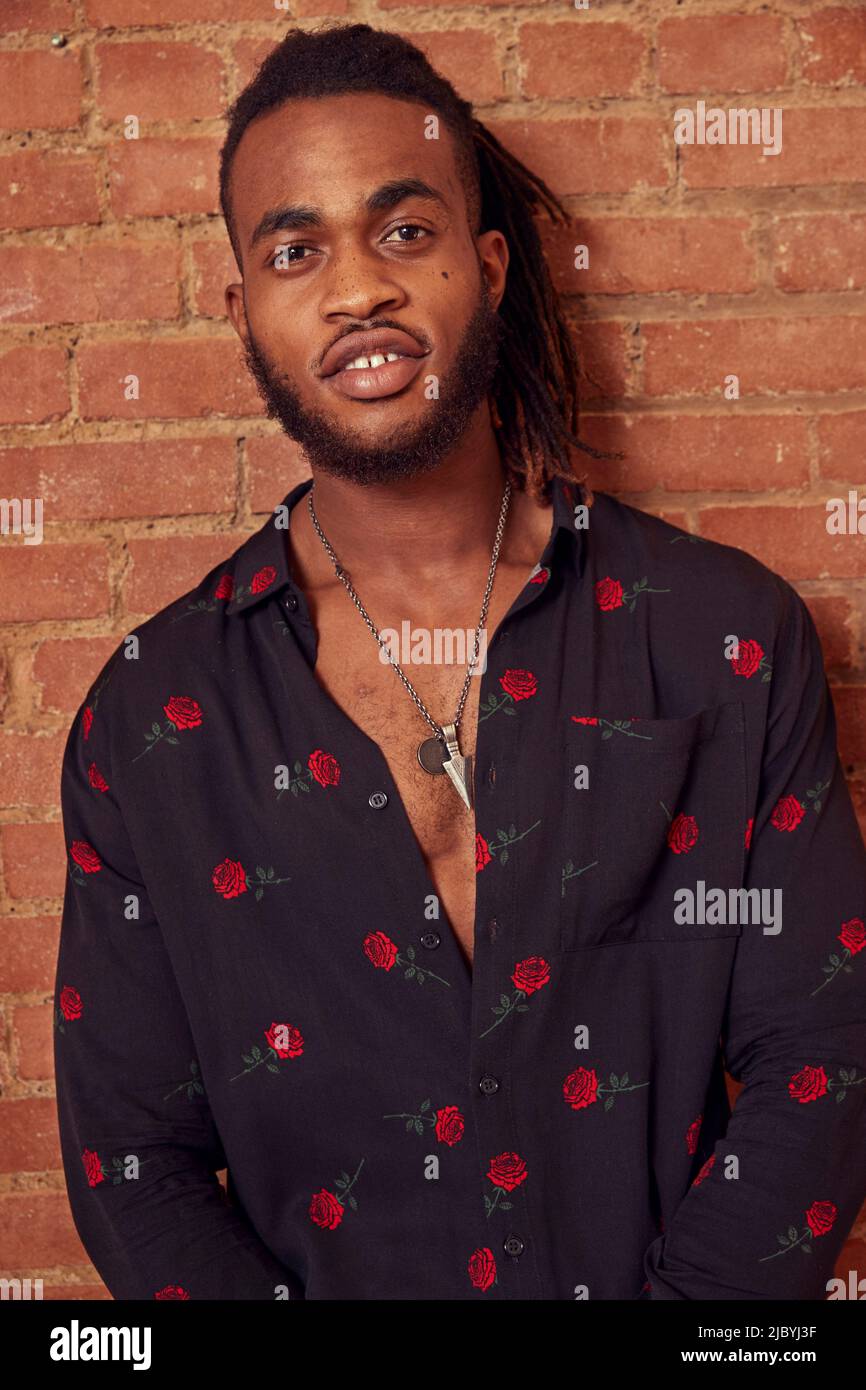 portrait of young ethnic man standing in front of exposed brick wall ...