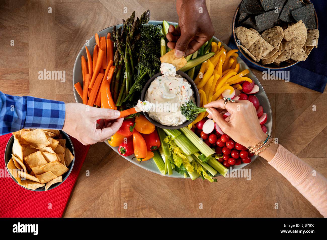Three people dipping in to veggie platter Stock Photo - Alamy