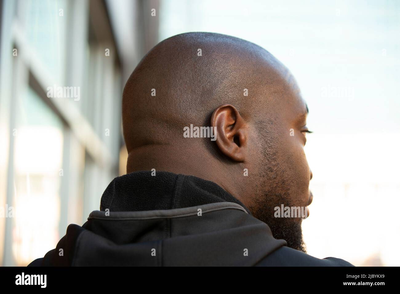 Rear view of young man with beard and a bald head standing outside ...