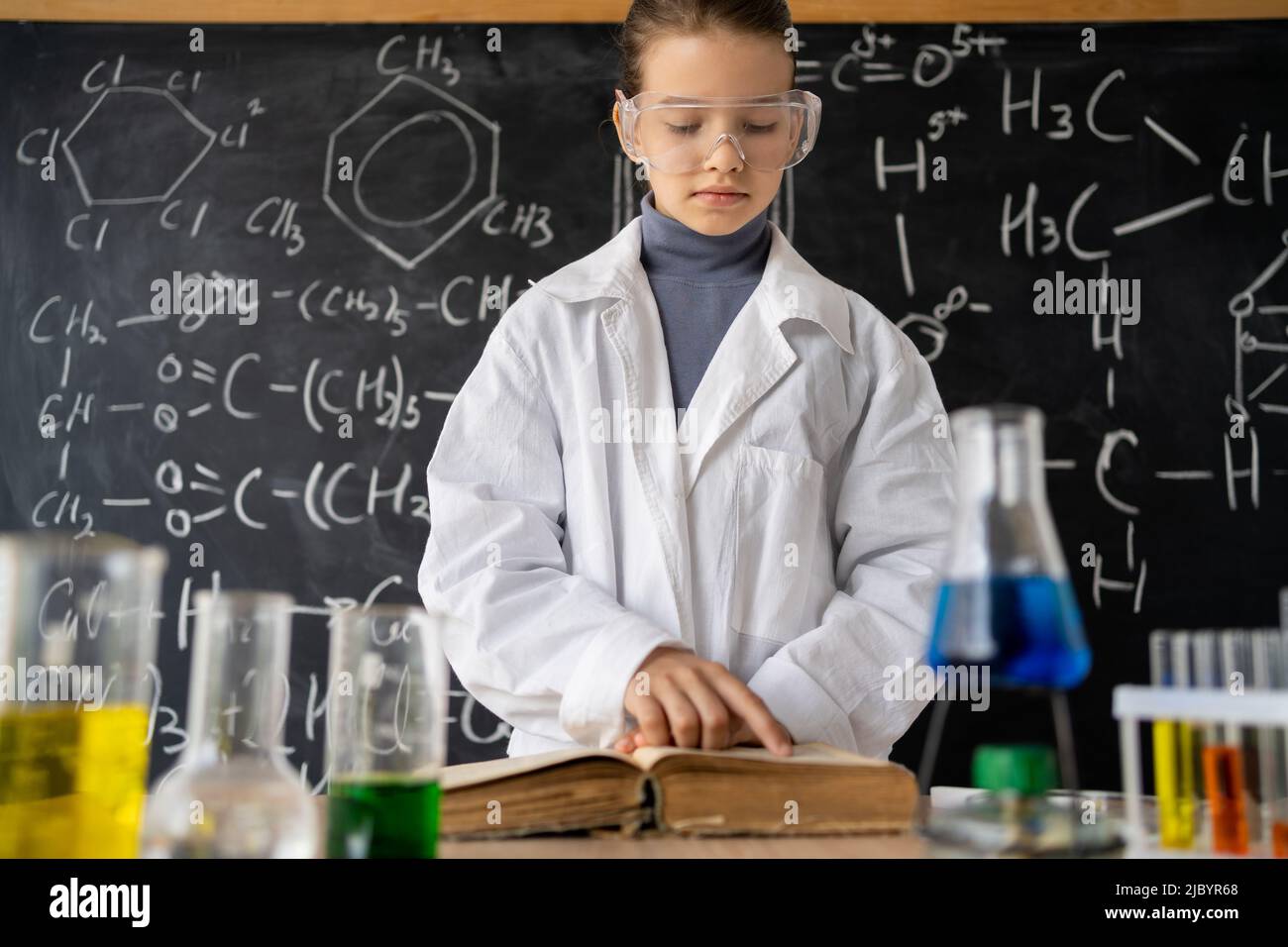 little scientist girl with glasses in lab coat mixing chemical liquids ...