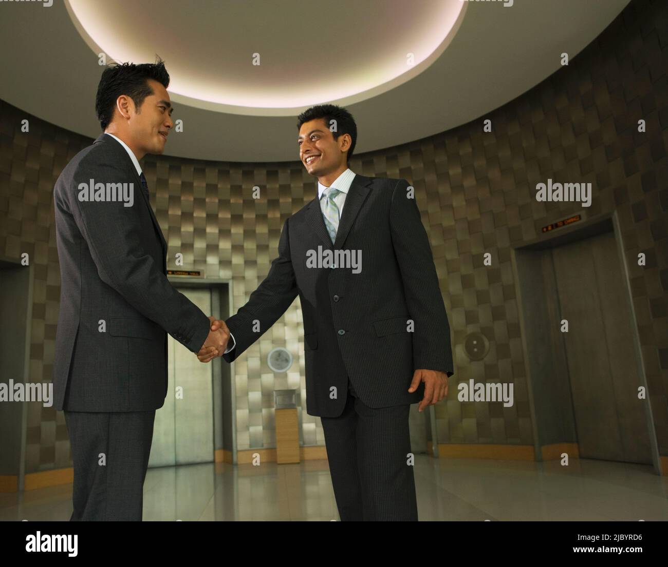Businessmen shaking hands in office lobby Stock Photo - Alamy