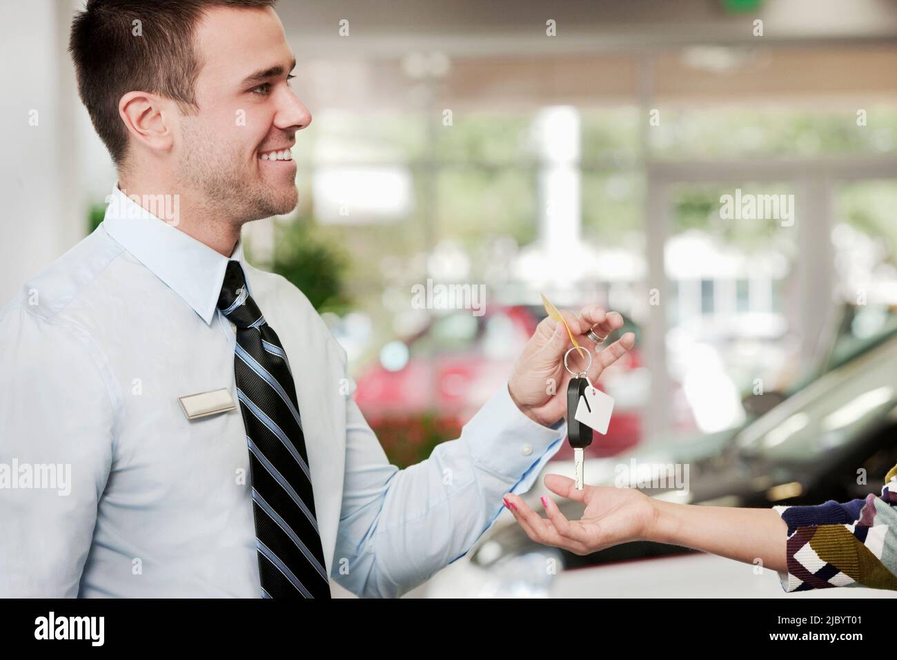 Man handing woman keys to new car in showroom Stock Photo - Alamy