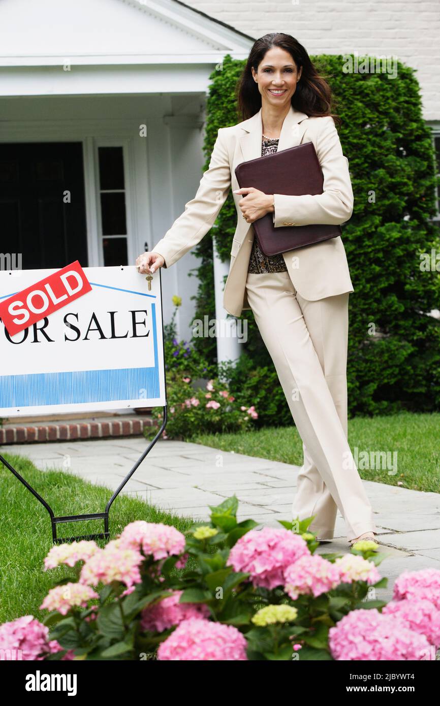 Hispanic female real estate agent and Sold sign in front of house Stock ...
