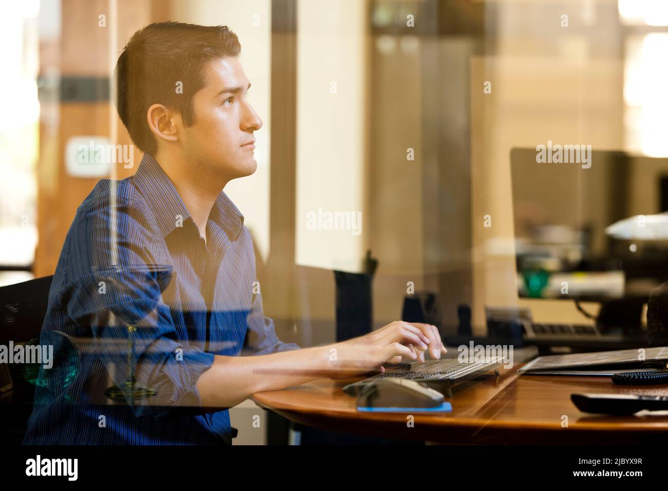 Hispanic man using computer behind glass Stock Photo - Alamy
