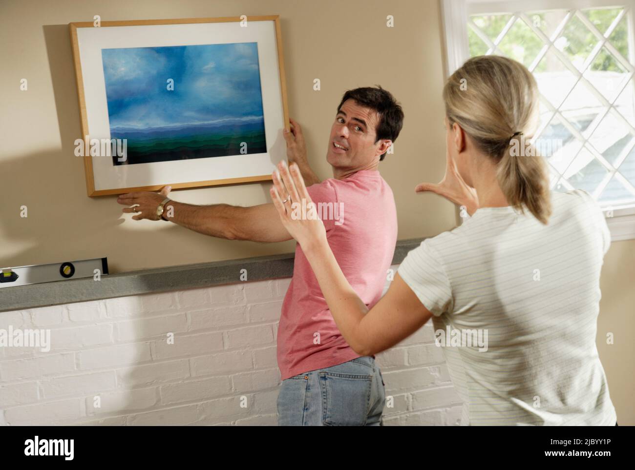 Couple hanging artwork over mantle Stock Photo - Alamy