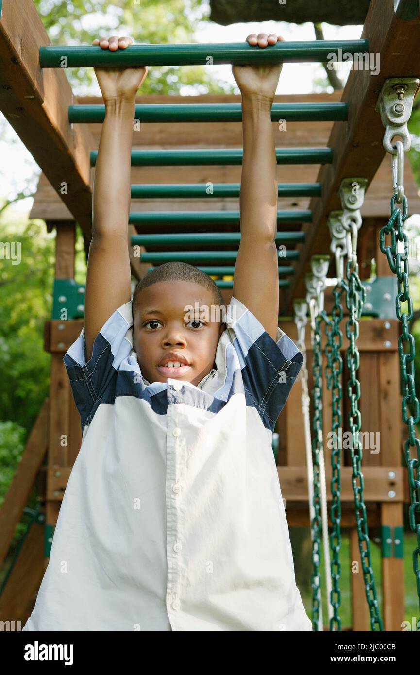 Young boy hanging from play structure Stock Photo - Alamy