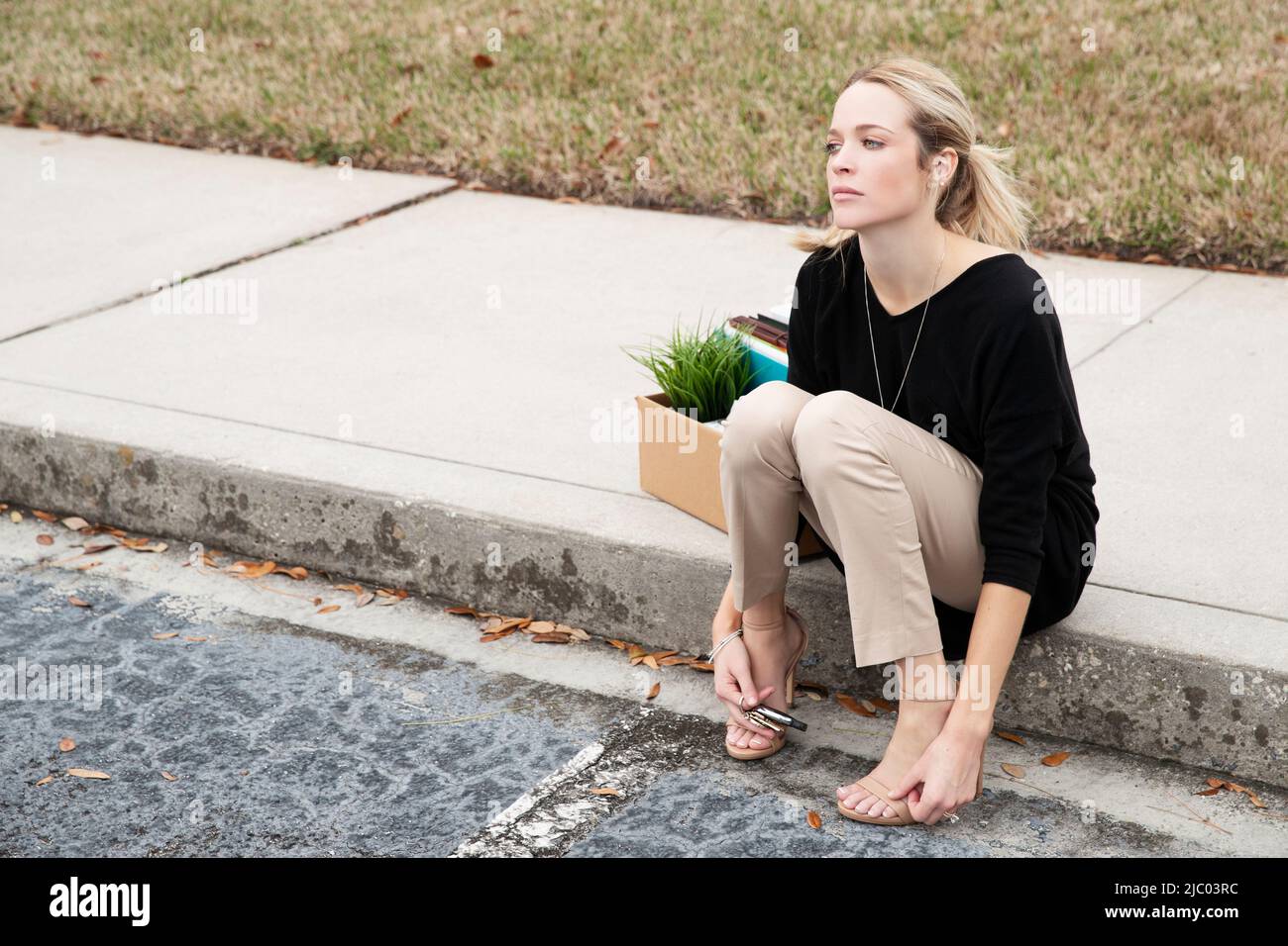 Distraught employee sitting on the curb with a box of her belongings ...