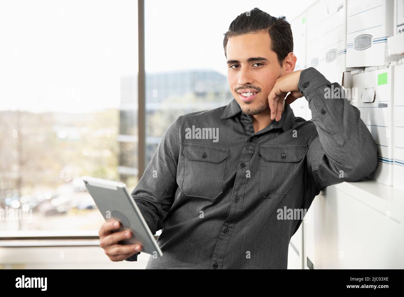 A millennial office employee leans up against a filing cabinet on ...