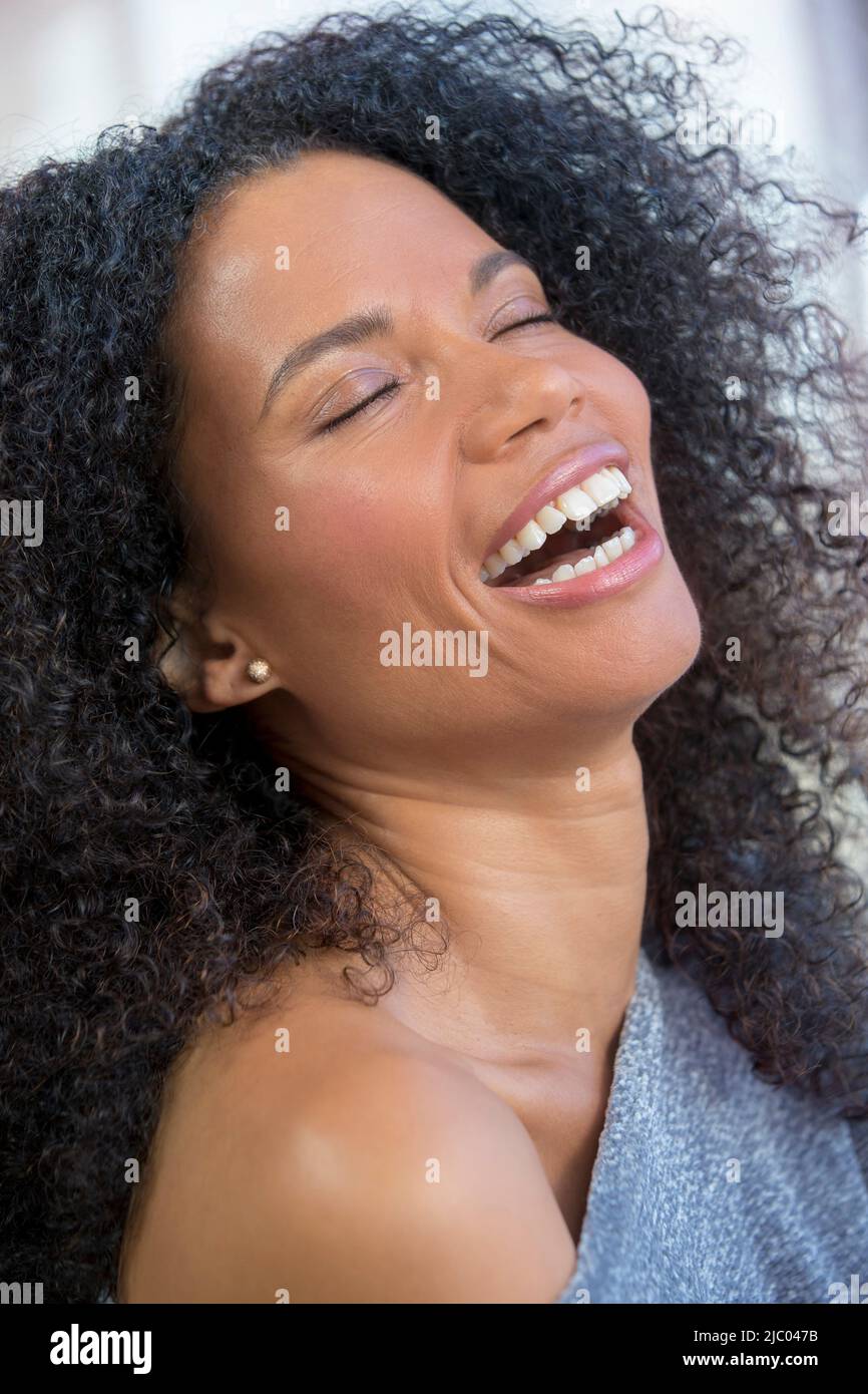 Vertical close up portrait of a mixed race, middle-aged woman laughing with her eyes closed ...