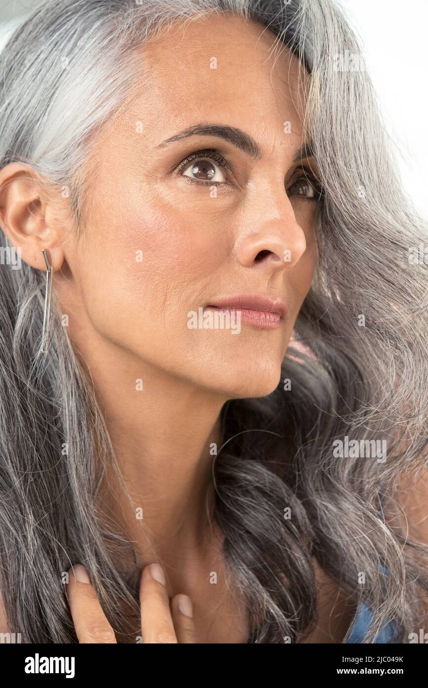 Close up of a middle-aged woman with gray hair, looking up off camera and brushing away her hair ...