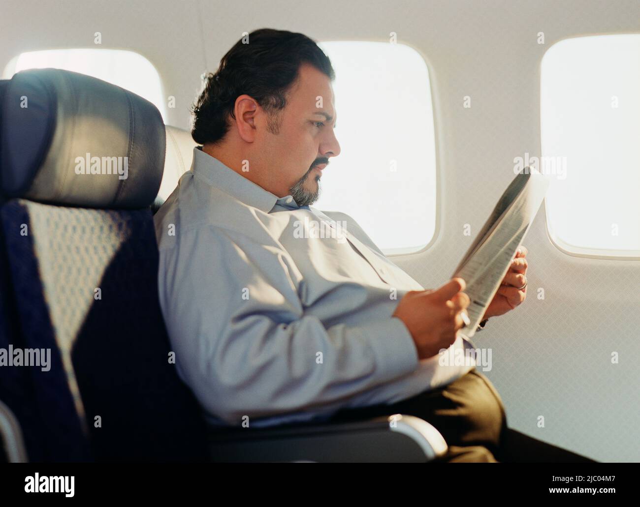 Overweight man reading newspaper on airplane Stock Photo - Alamy