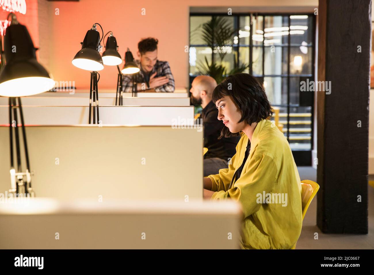 group of young adults at individual workstations in co-working space ...