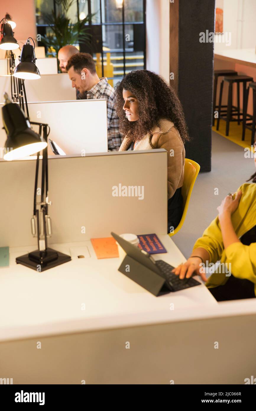 group of young adults at individual workstations in co-working space ...