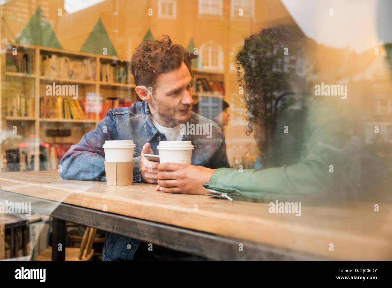 Friends sitting in window of cafe with mobile phone Stock Photo - Alamy