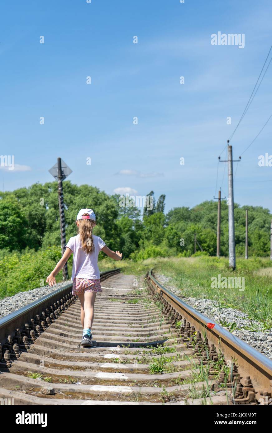 Rear view of little girl walking on railroad track against clear blue ...