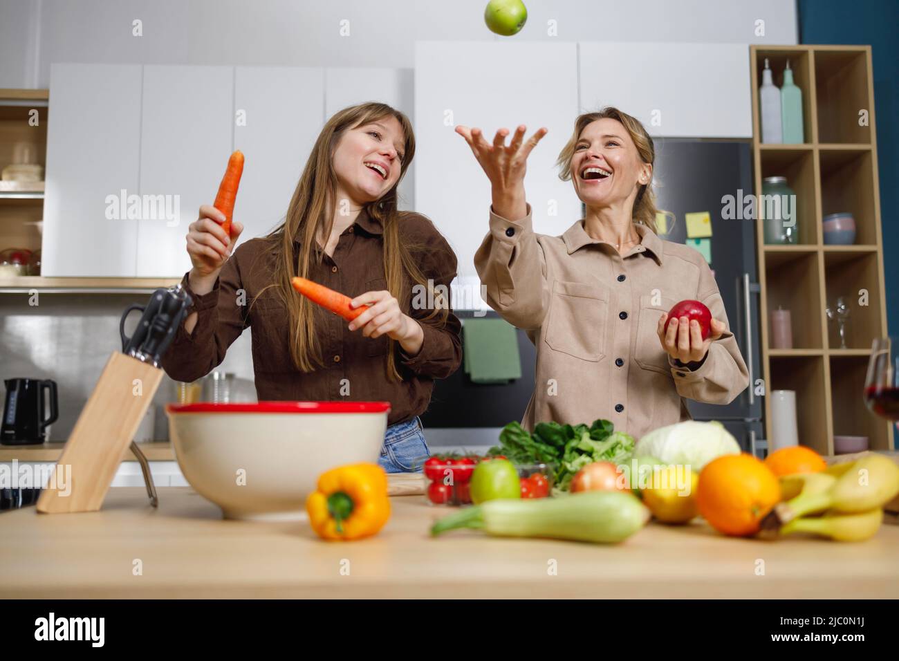 Mature mother and her adult daughter have fun while cooking in the ...