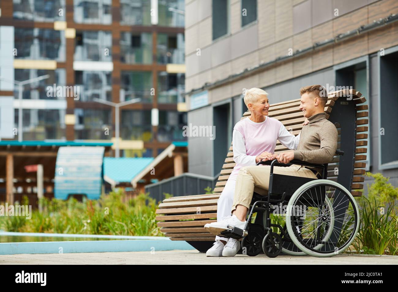 Positive mature blond rehabilitation worker sitting on wooden bench on ...