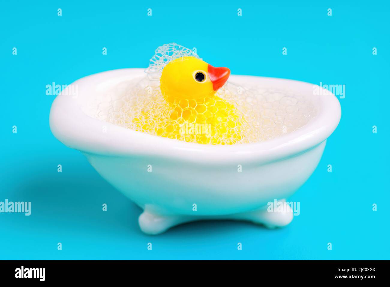 Toy yellow duck in a miniature white bathtub covered with soap bubbles ...