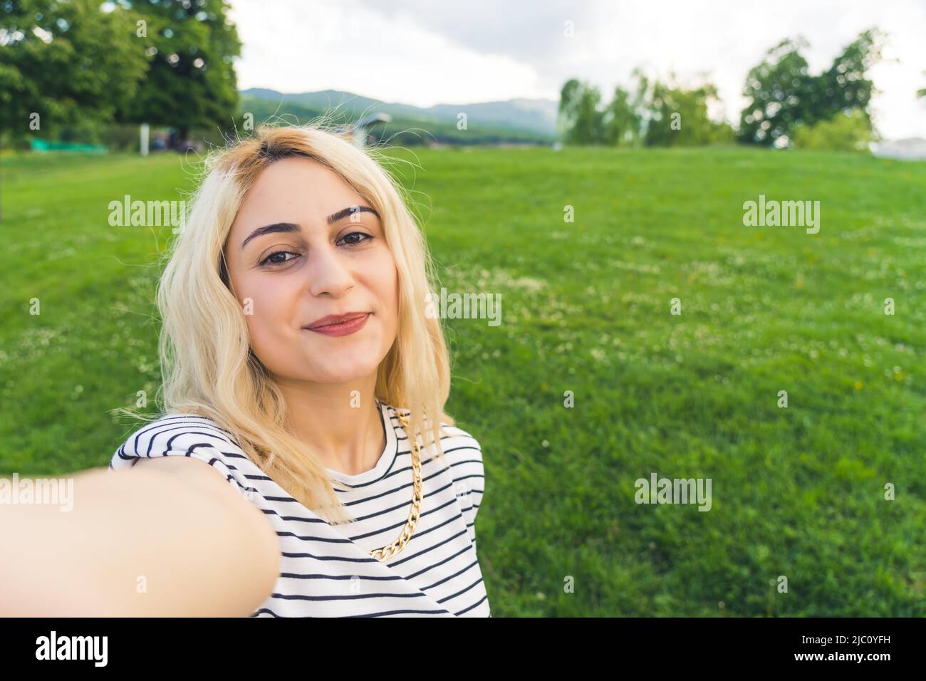 pretty Caucasian girl taking a selfie and smiling. green grass park ...