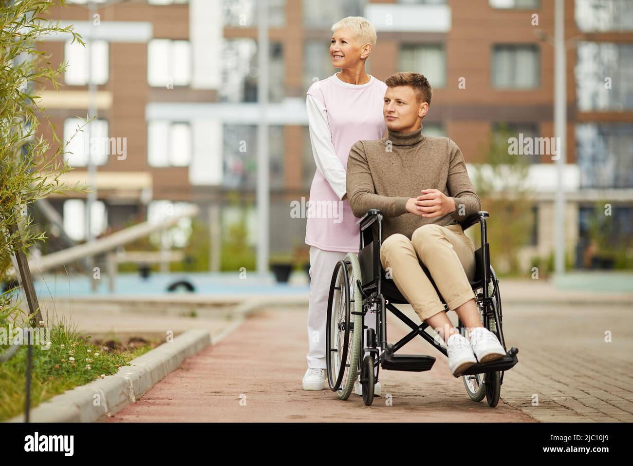 Smiling attractive blond lady in uniform pushing wheelchair with ...
