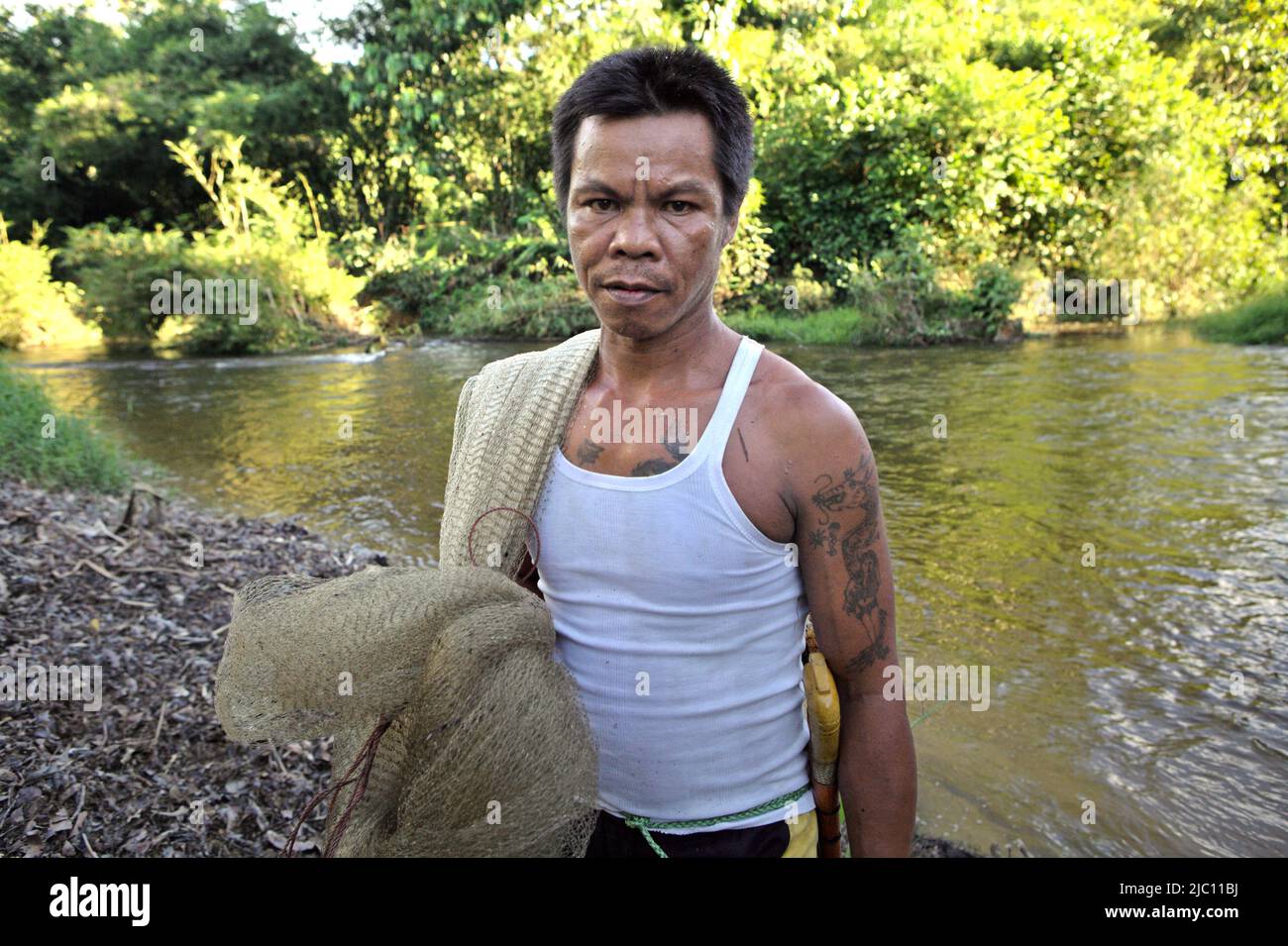Portrait of a man carrying a fishing net on riverbank in Sungai Utik ...