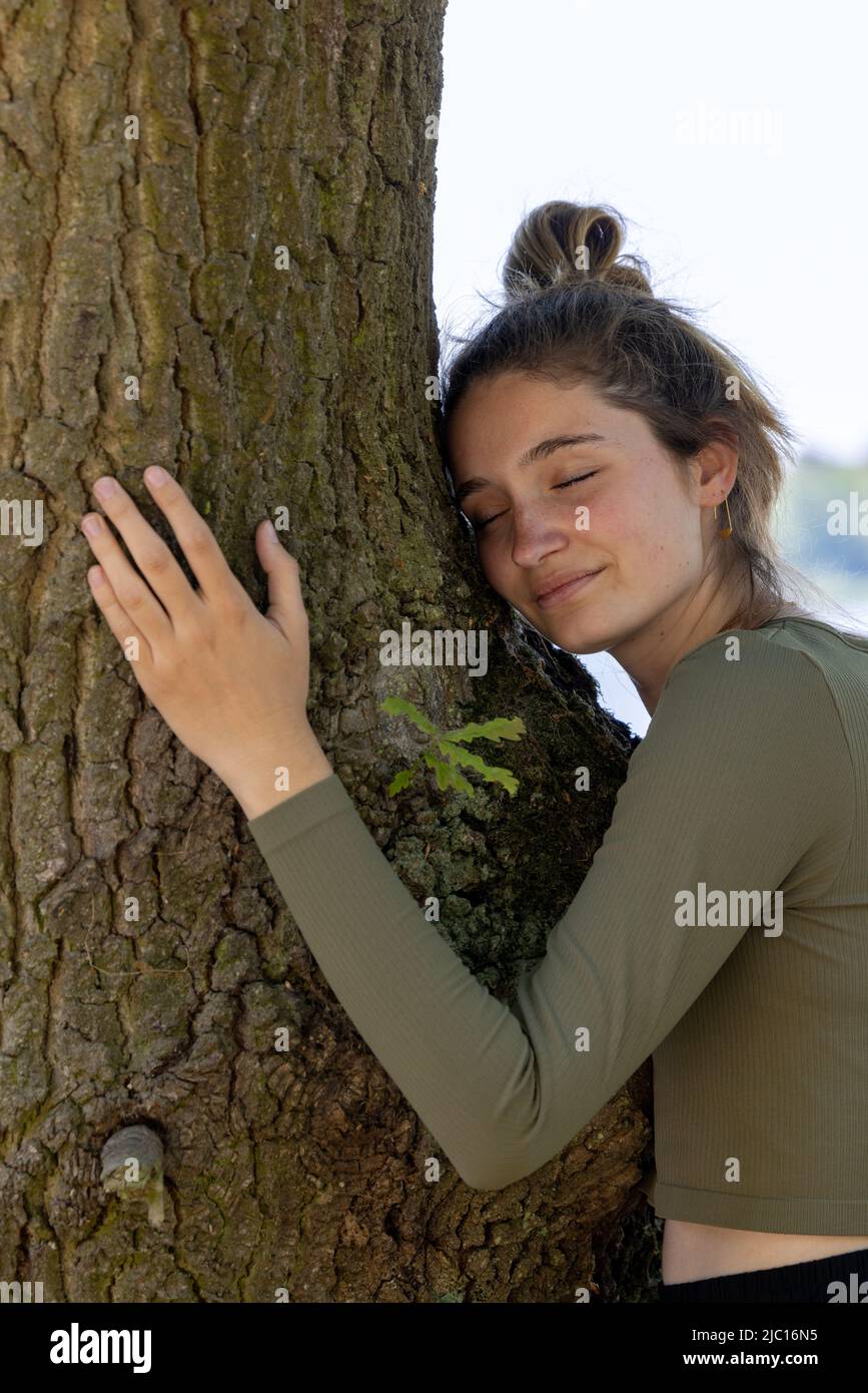 Contented young woman hugging a large tree with a blissful expression ...